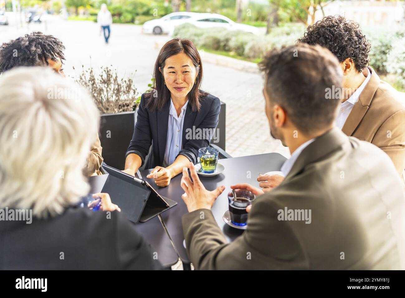 Chinese businesswoman talking with colleagues using tablet and drinking ...