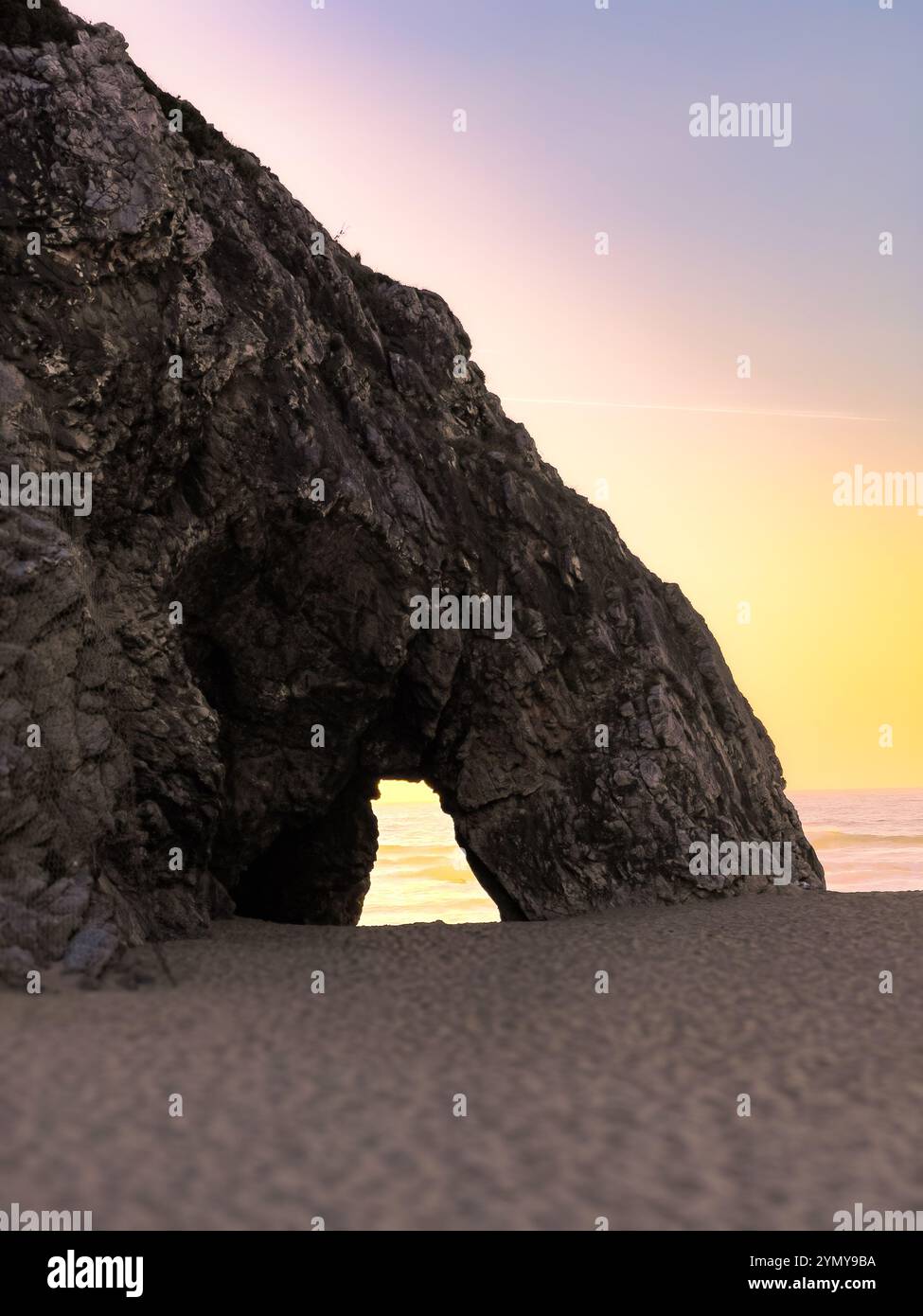 A rocky archway frames a golden sunset on the beach Stock Photo - Alamy