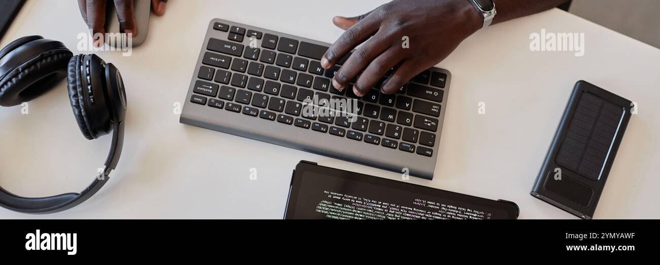 Close-up of hands typing code on wireless keyboard while multitasking with gadgets on clean ...