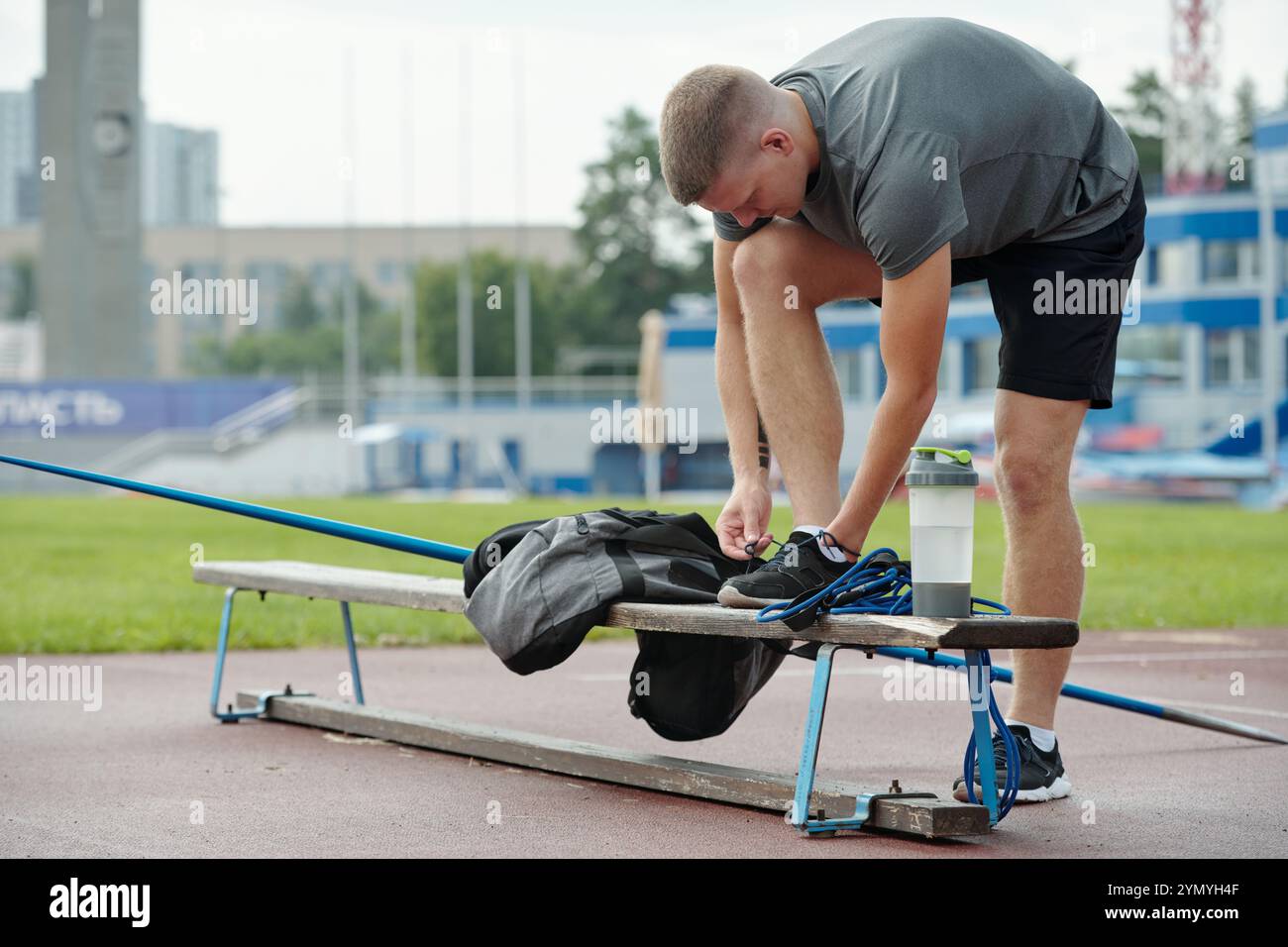 An athlete preparing for training by sitting on bench and tying ...
