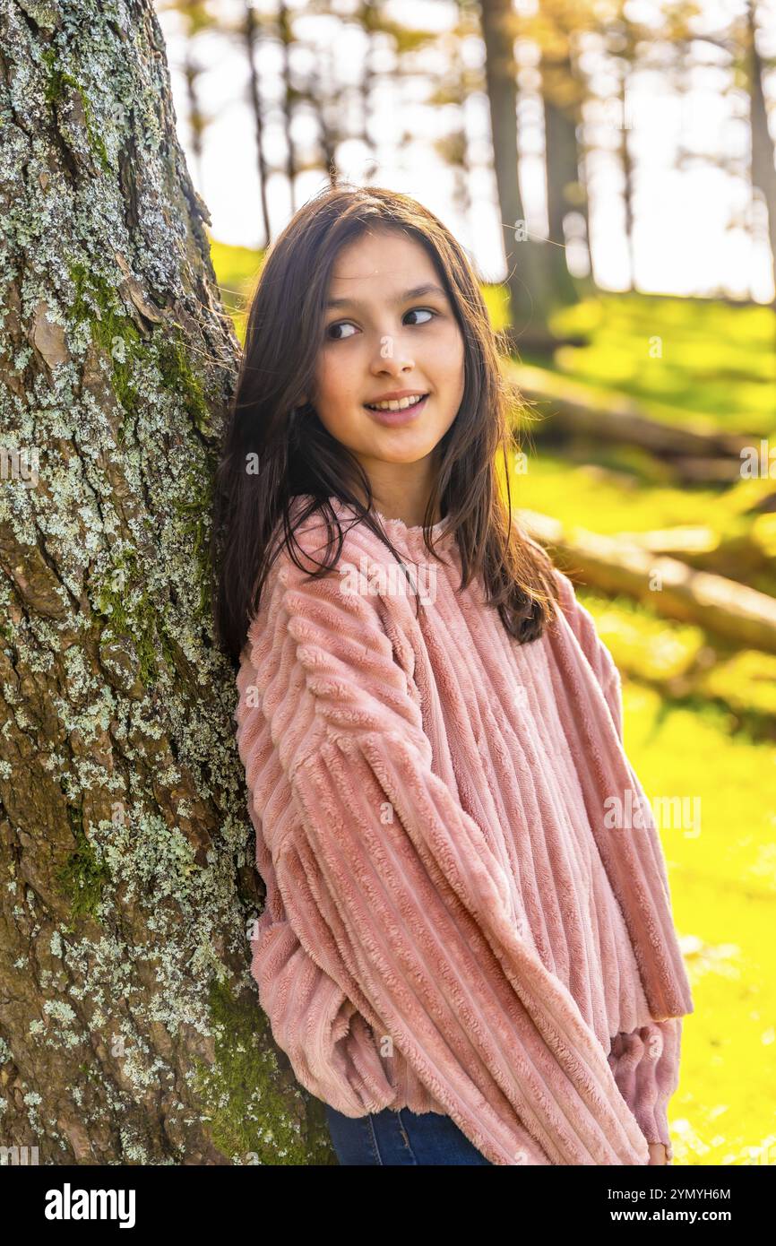 Vertical side view portrait of a caucasian cute girl leaning in a tree ...