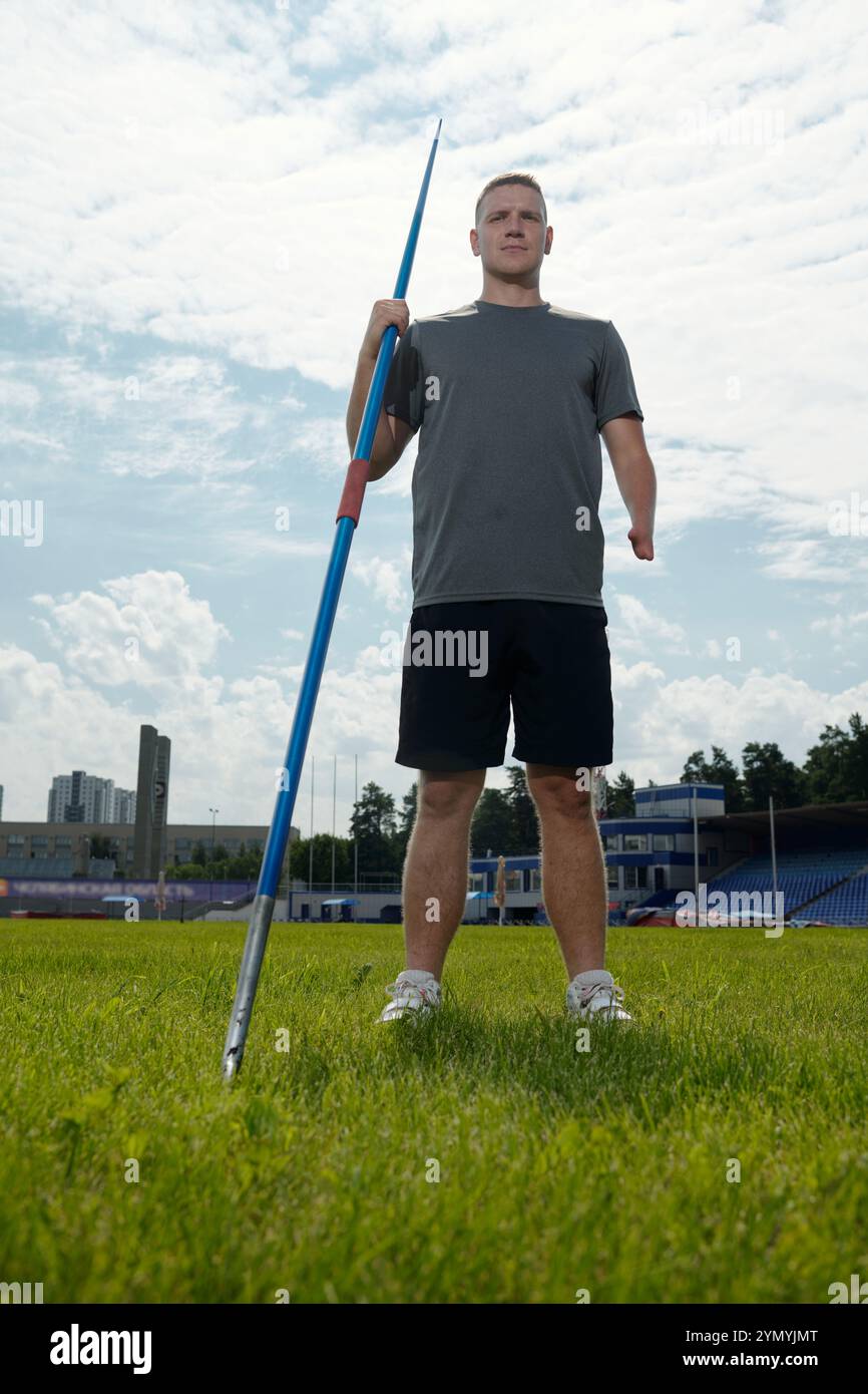 Athlete holding javelin on sports field with stadium and sky in ...