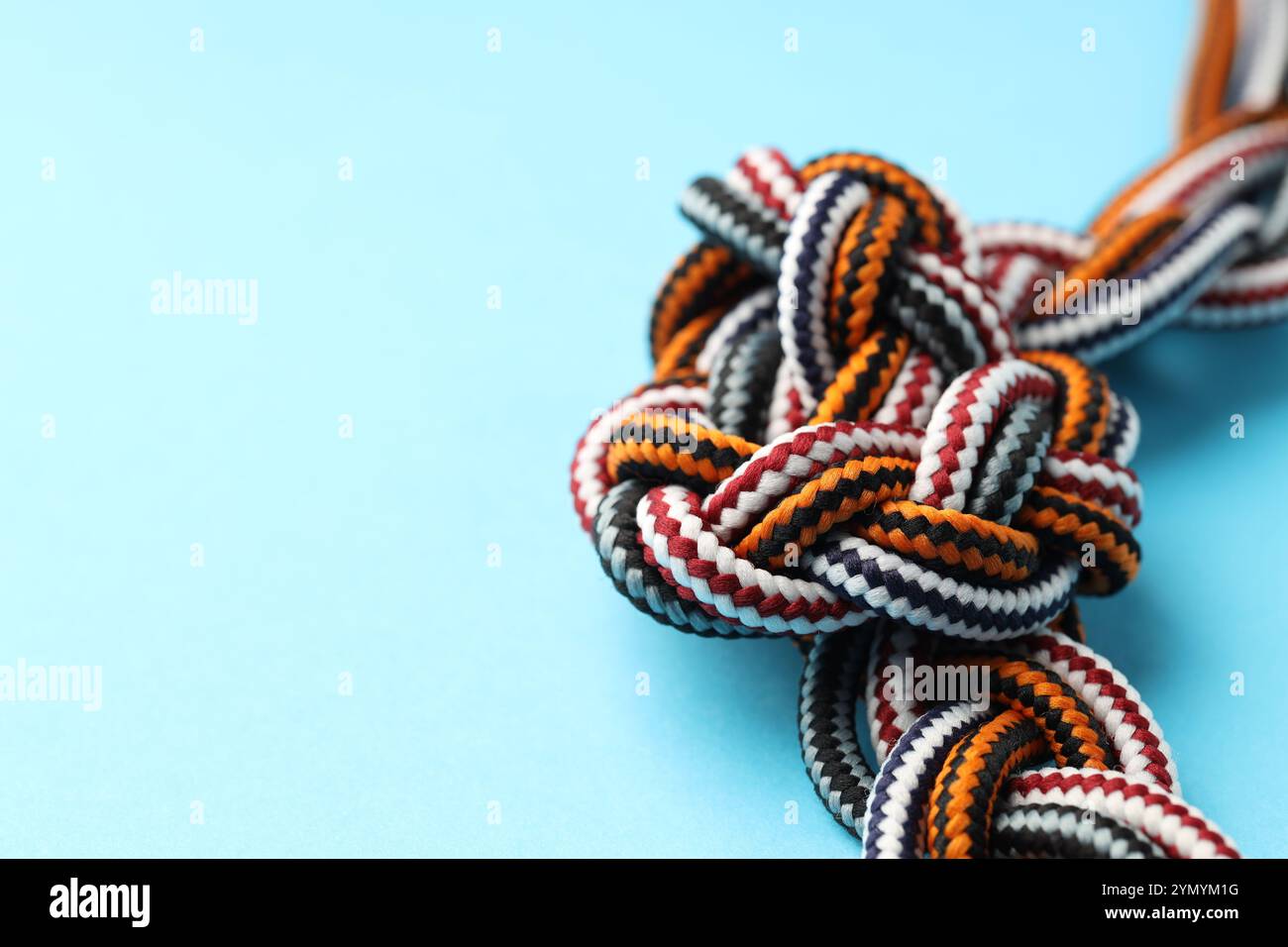 Colorful ropes tied in knot on light blue background, closeup and space ...