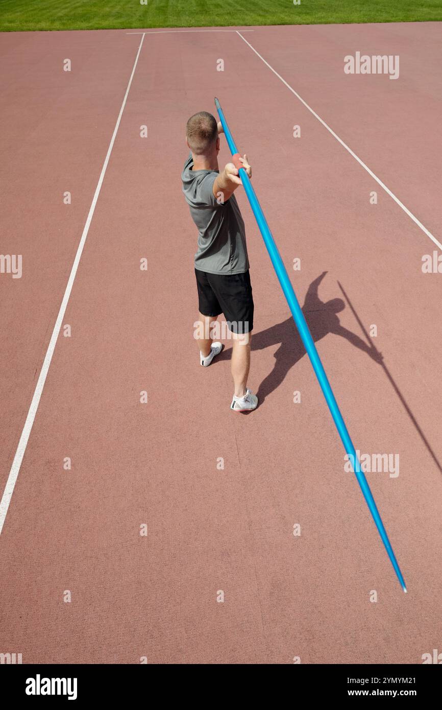 Athlete preparing for javelin throw on track field with clear sky and ...