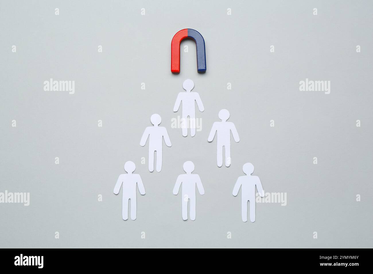 Magnet attracting paper cutouts of humans on light grey background ...