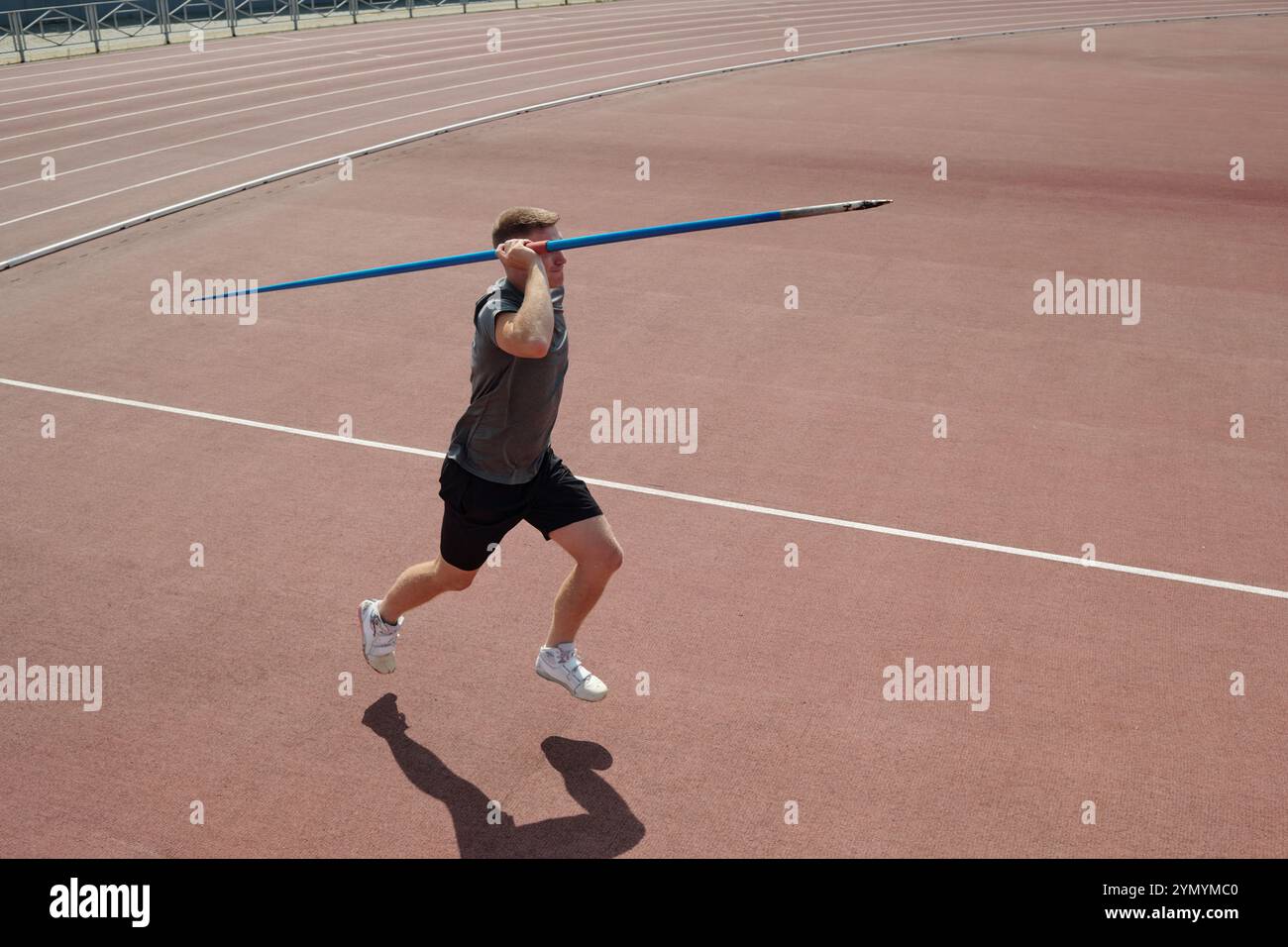 Athlete running on red track field holding javelin above shoulder and ...