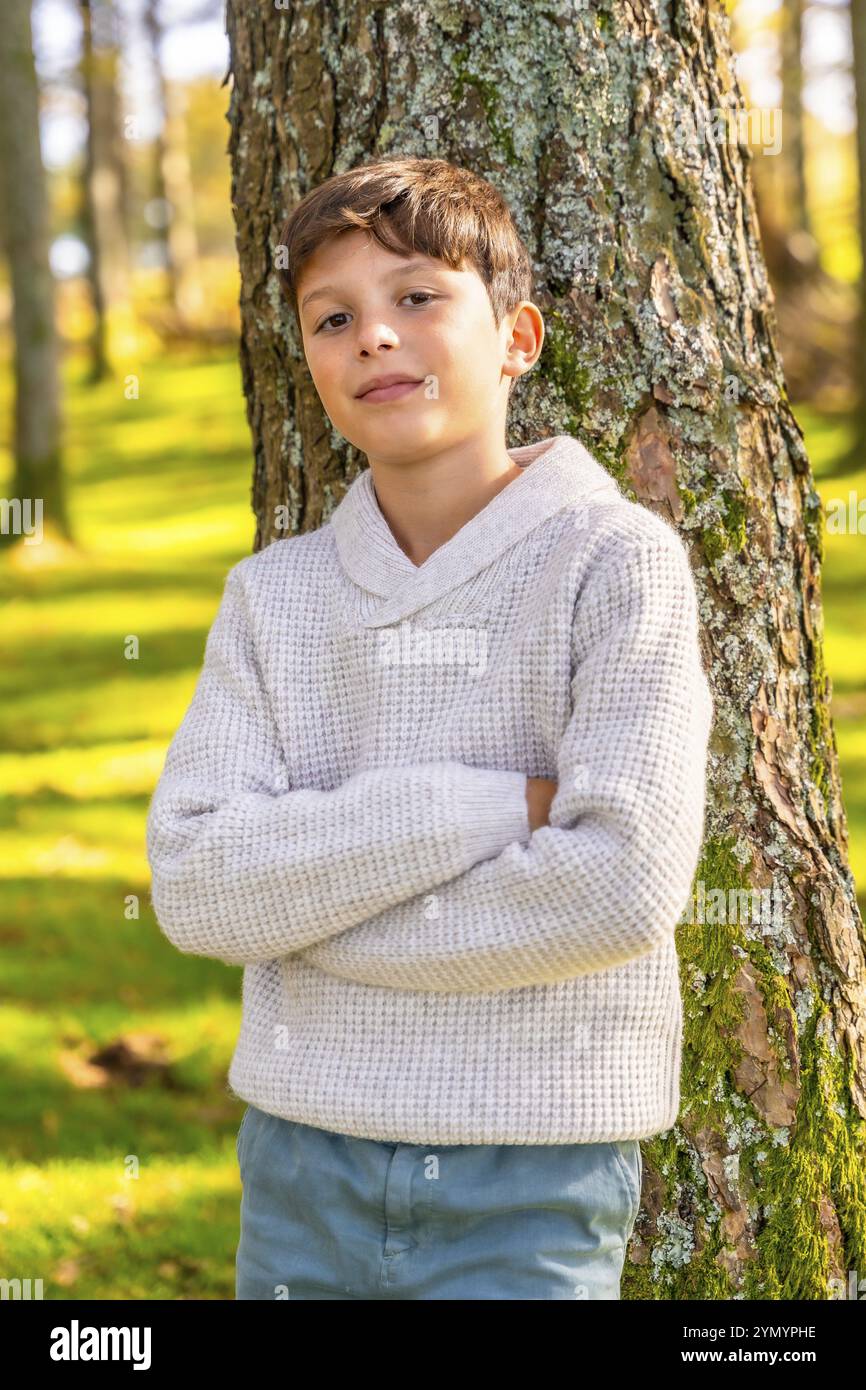 Vertical portrait of a caucasian young confident boy leaning on tree ...