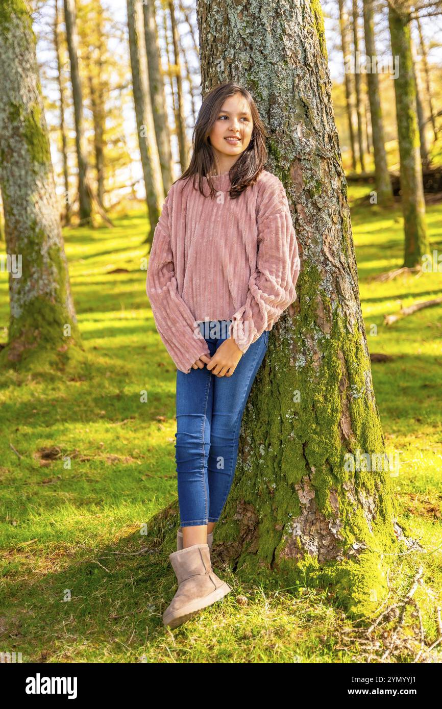 Vertical full length portrait of a cute teen girl leaning on tree trunk ...