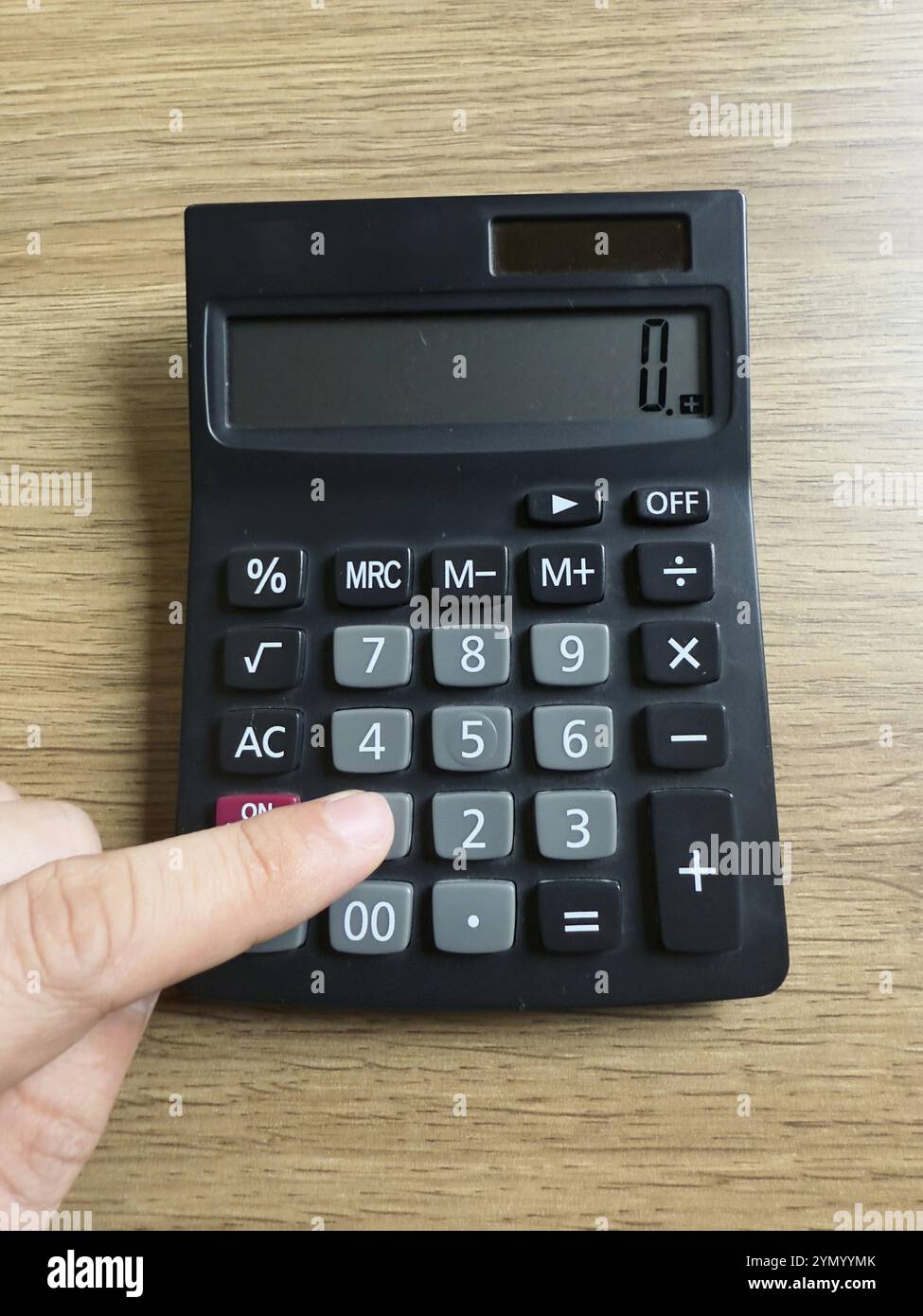 A hand pressing a button on a black calculator with a digital display ...