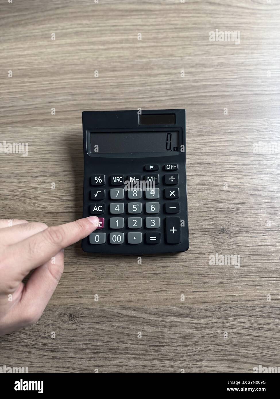 A hand pressing the AC button on a black calculator with the display ...