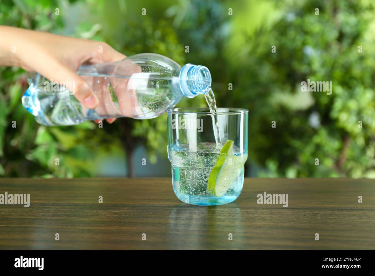 Woman pouring soda water from bottle into glass at wooden table ...