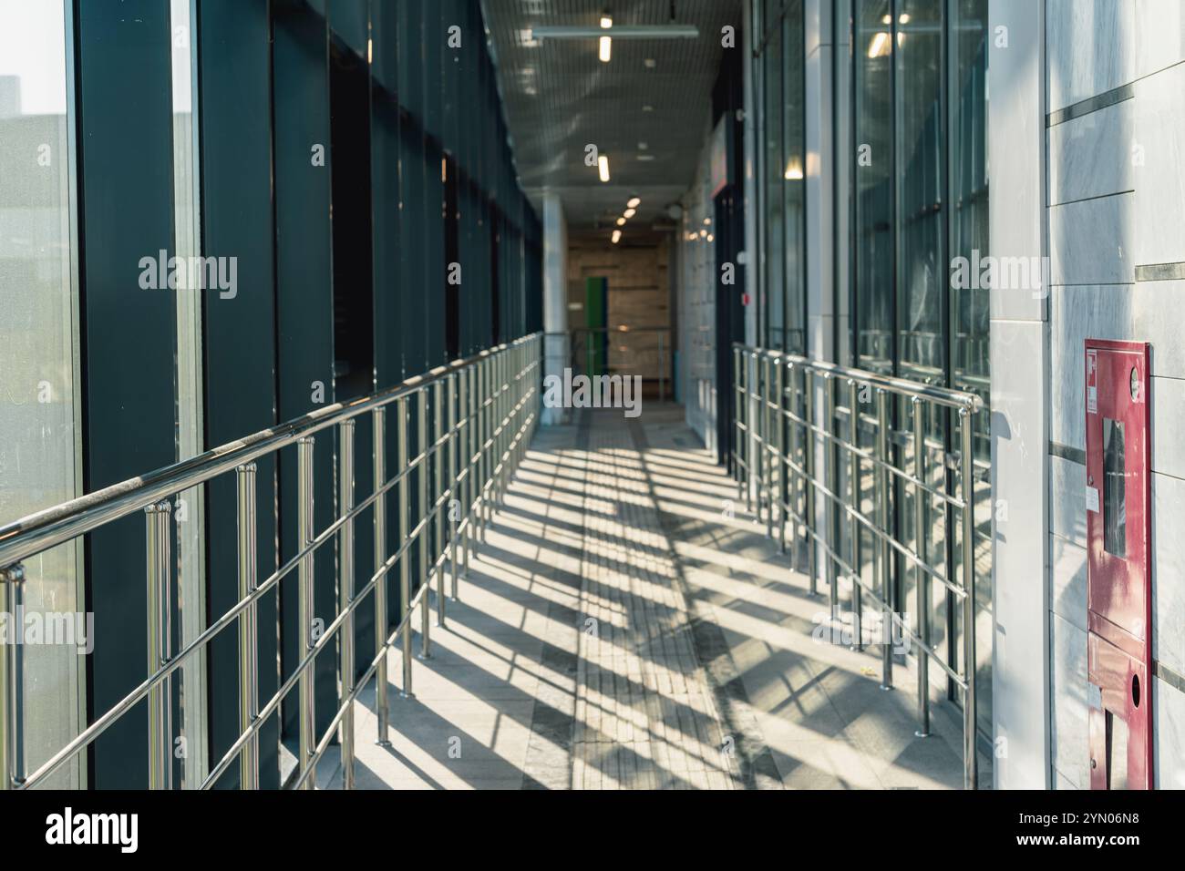 A sunlit corridor in a modern building featuring metal railings and ...