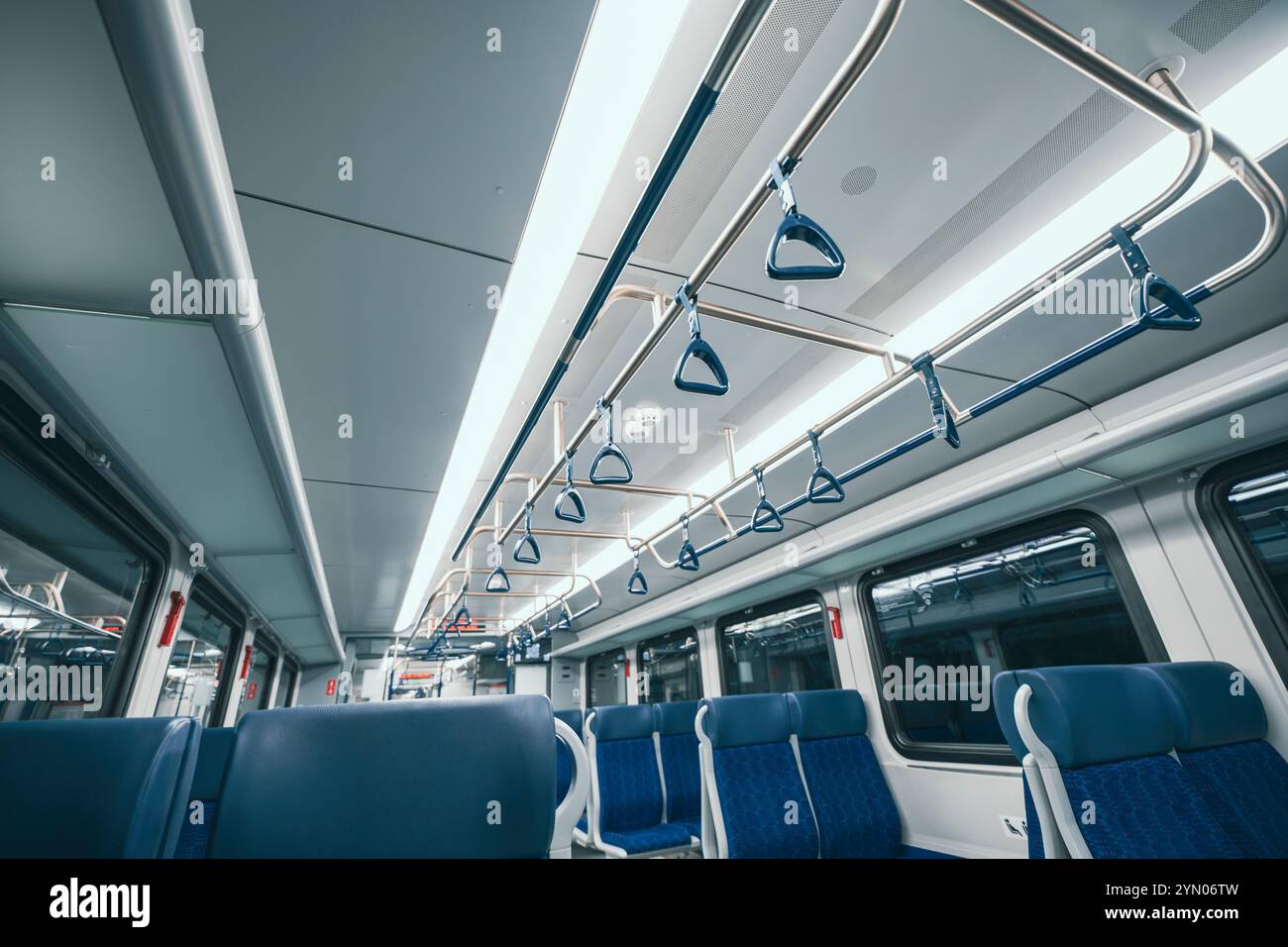 Interior view of an empty train with blue seats and overhead handrails ...