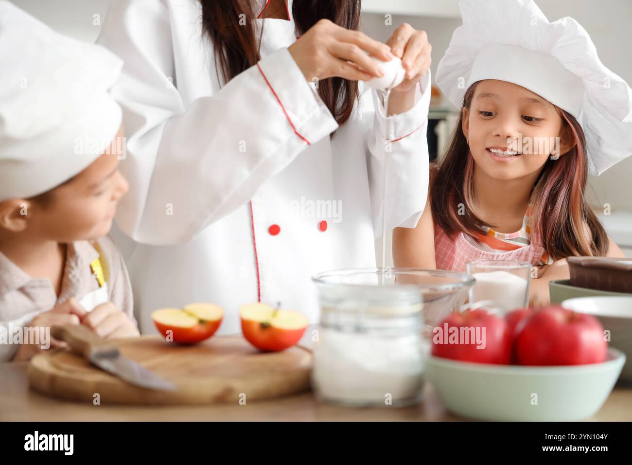 Female Asian chef with her little children breaking egg in kitchen ...