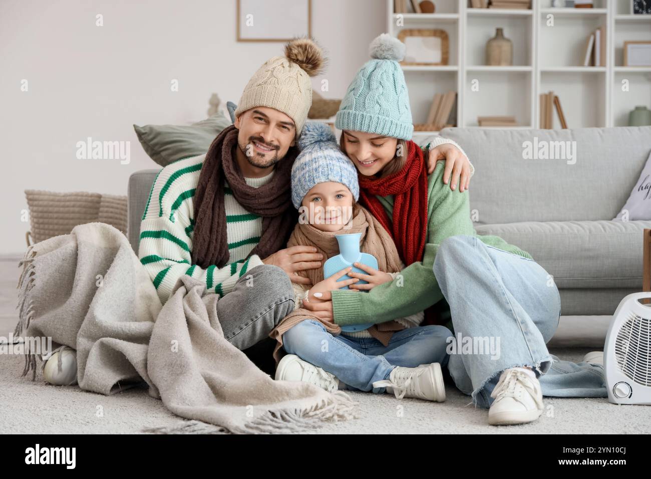 Frozen family with hot water bottle sitting near electric fan heater at ...