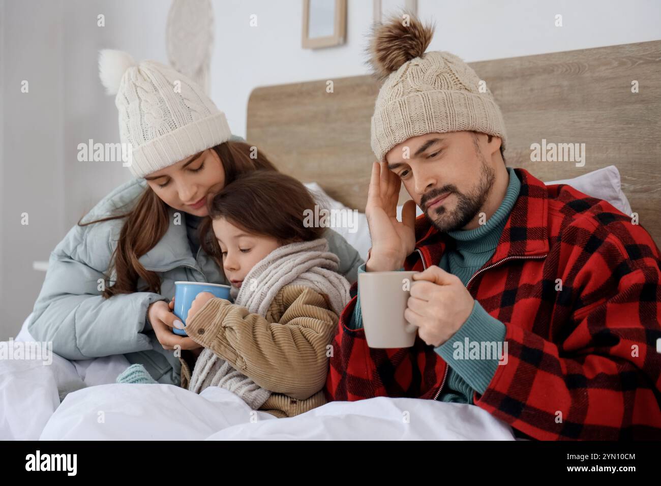 Frozen family with cups of tea and lack of heating lying in bedroom ...