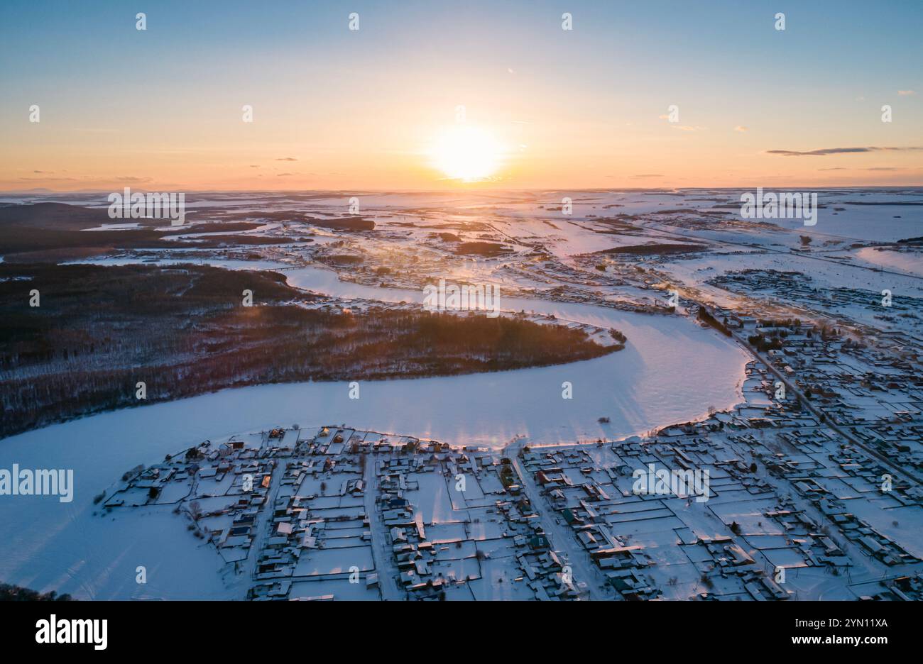 Sunrise over snowy landscape revealing a river and quiet village during ...