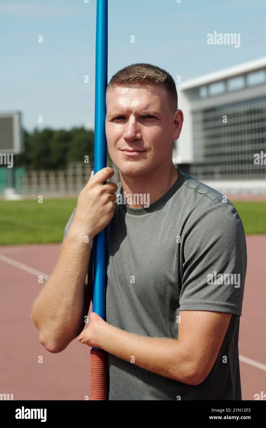 Portrait of a man gripping a pole on track with a modern building in ...