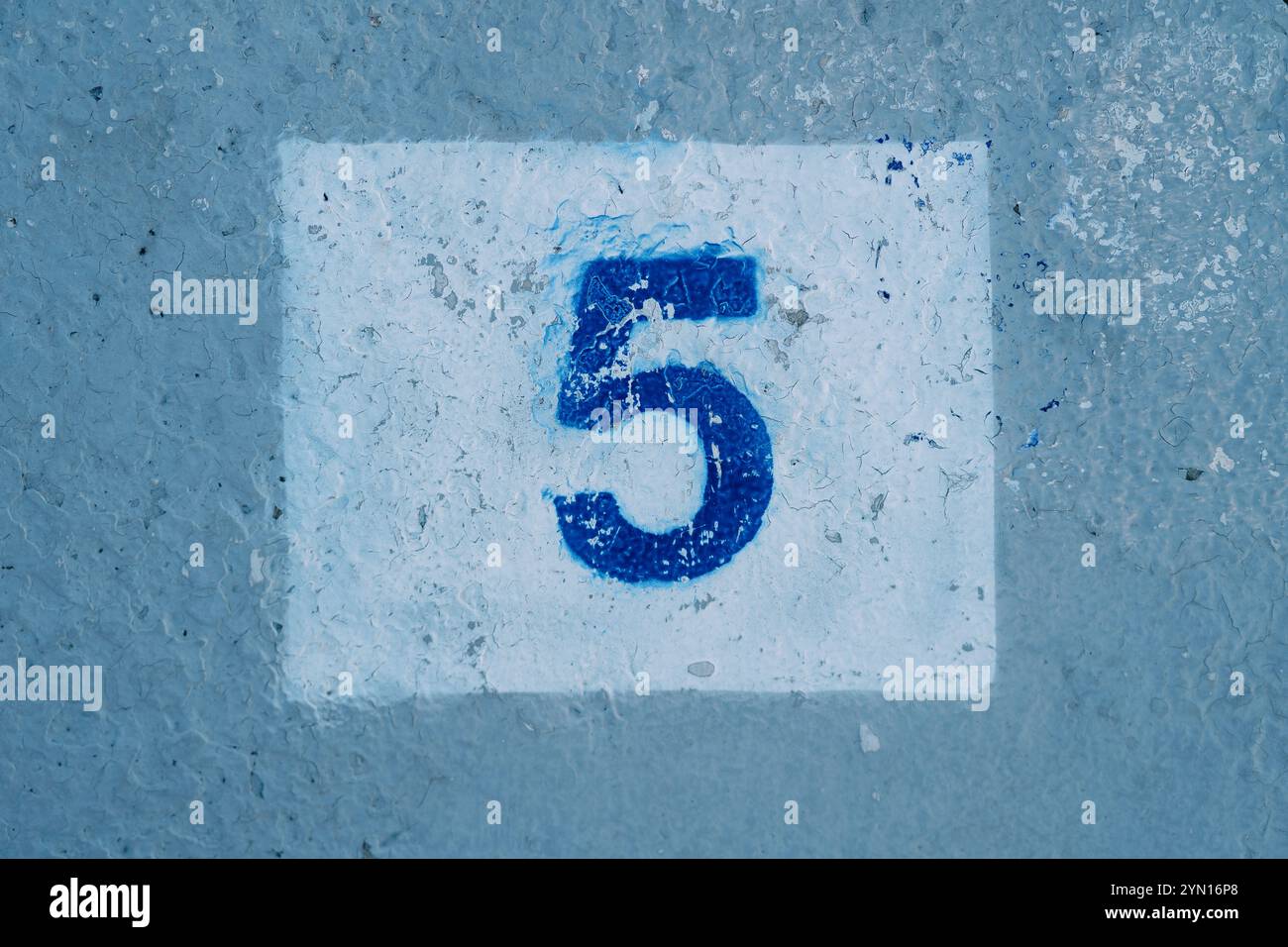 Number five with scratched paint drawn on a blue wall in a rectangle ...