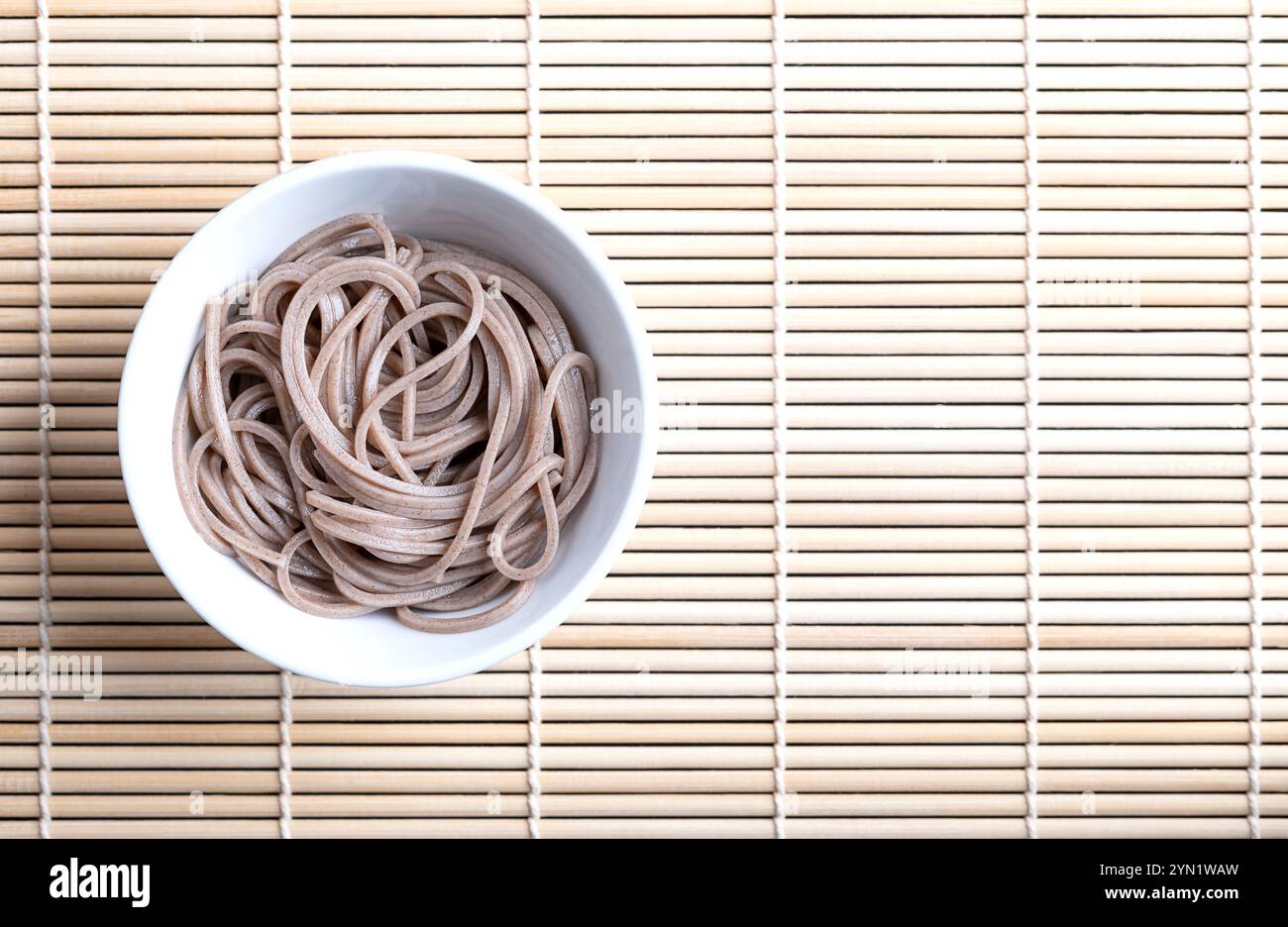 Chilled, boiled soba noodles in a white bowl, placed on a bamboo mat ...