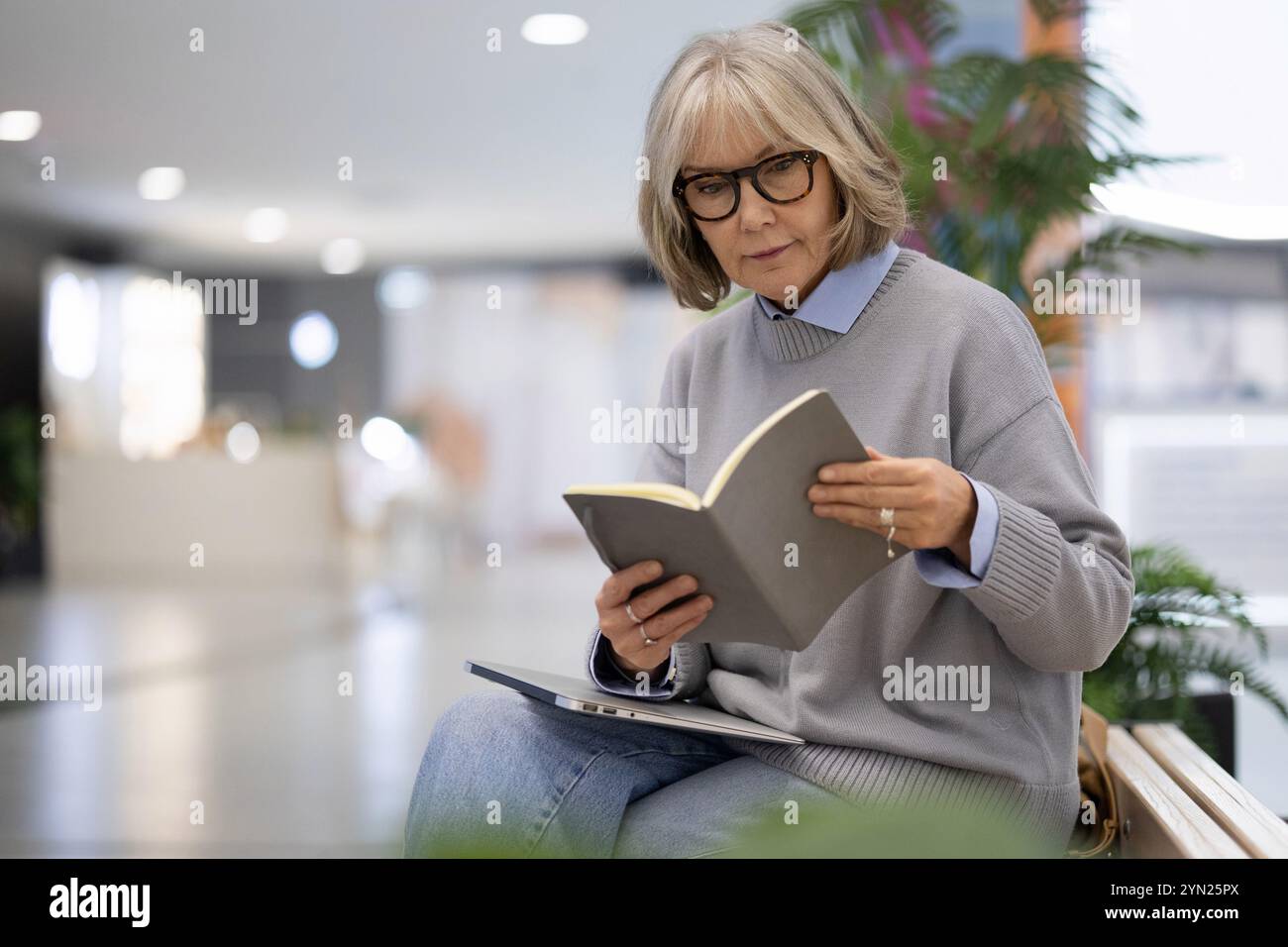 A woman enjoys reading a book in a modern indoor space surrounded by ...