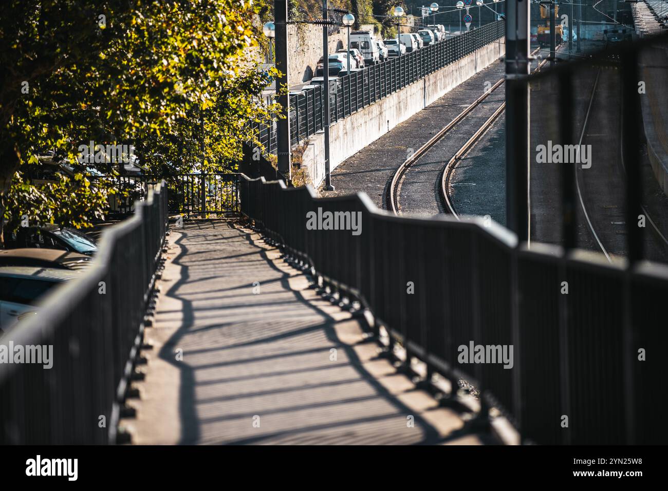 A pedestrian walkway with metal railings casting shadows, next to tram ...