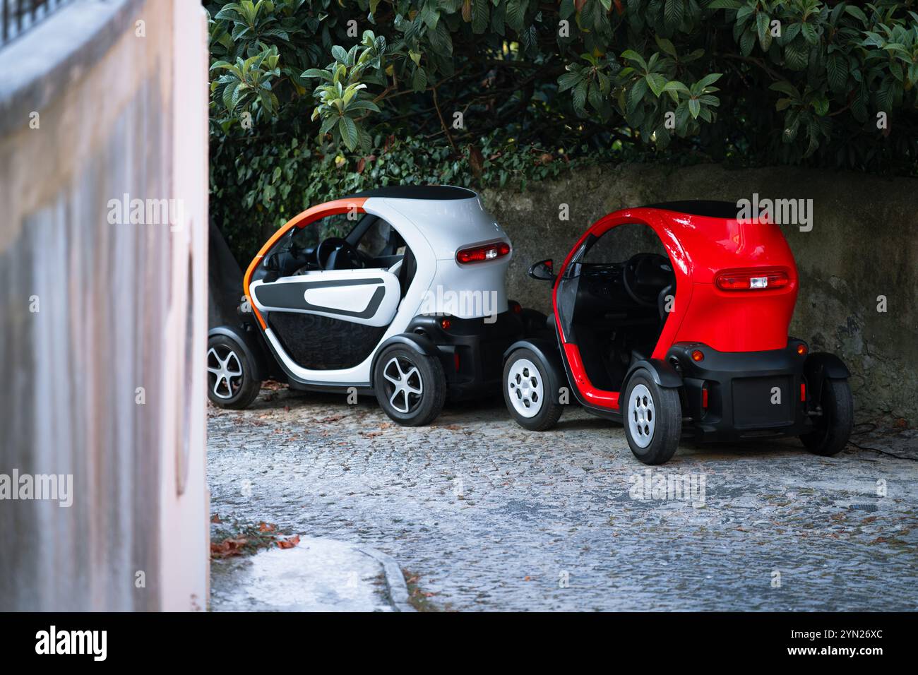 Two compact electric microcars parked side by side on a cobblestone ...