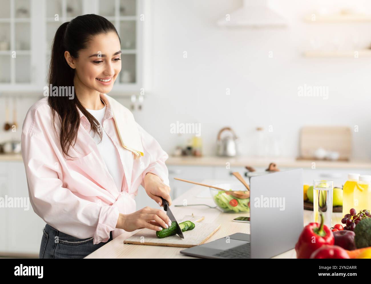 Woman cooking salad and using personal computer at kitchen Stock Photo ...