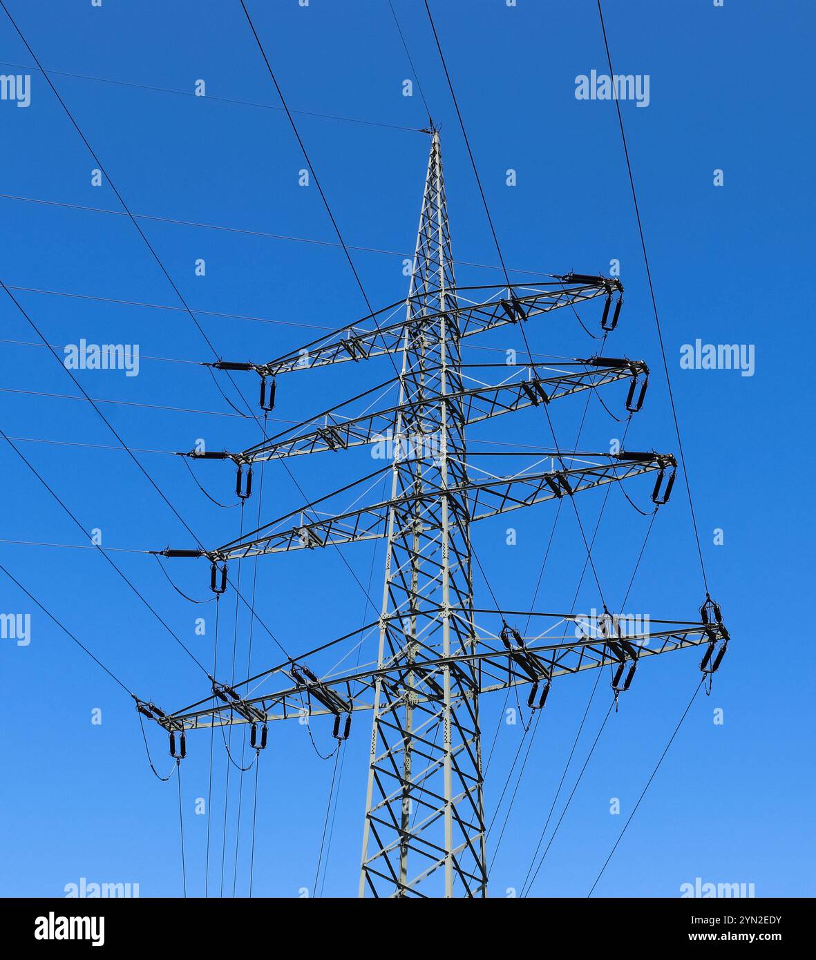 A very large electricity pylon with many cables in front of a blue sky ...