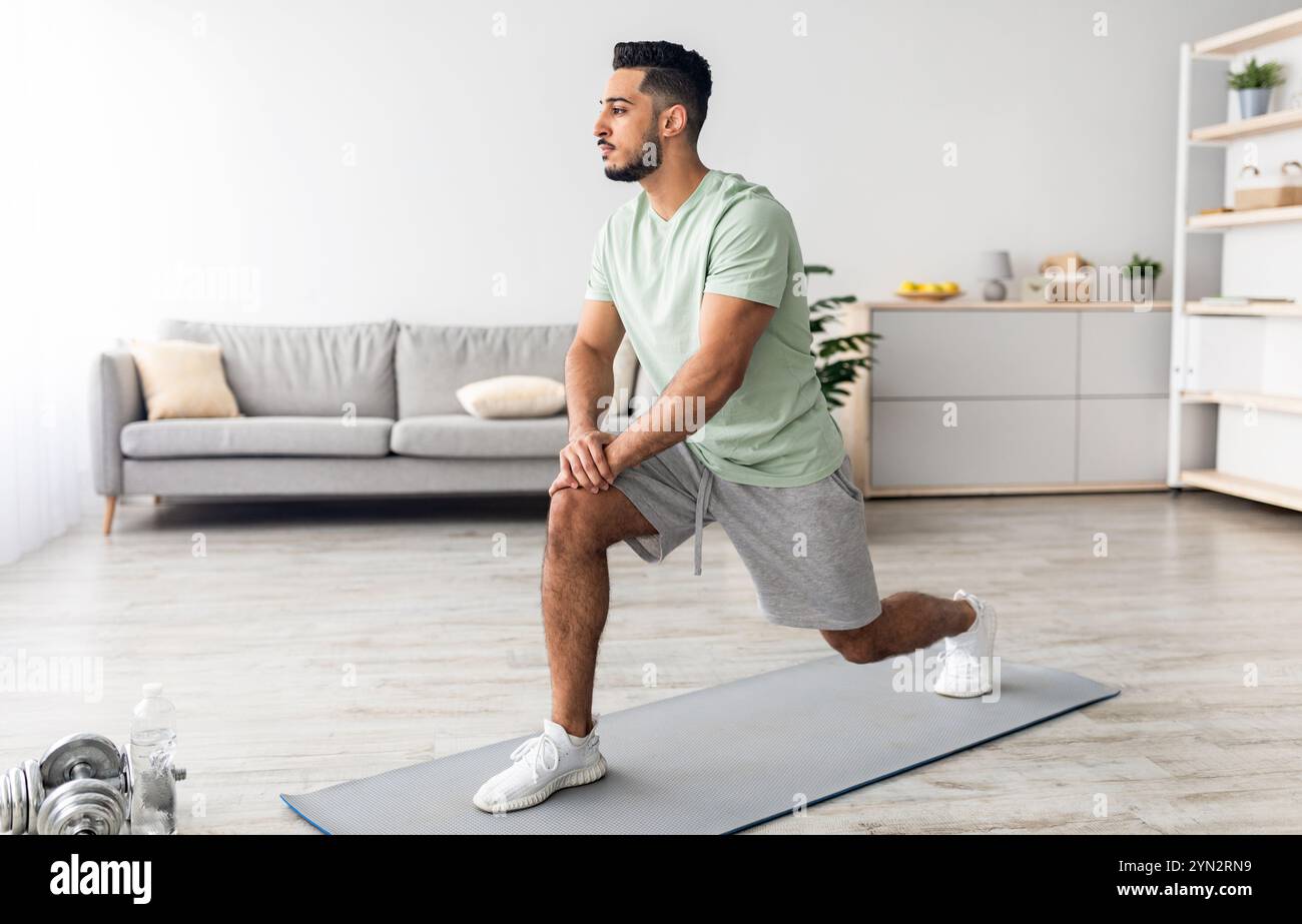 Fit young Arab guy making lunge, doing strength exercises, working out ...
