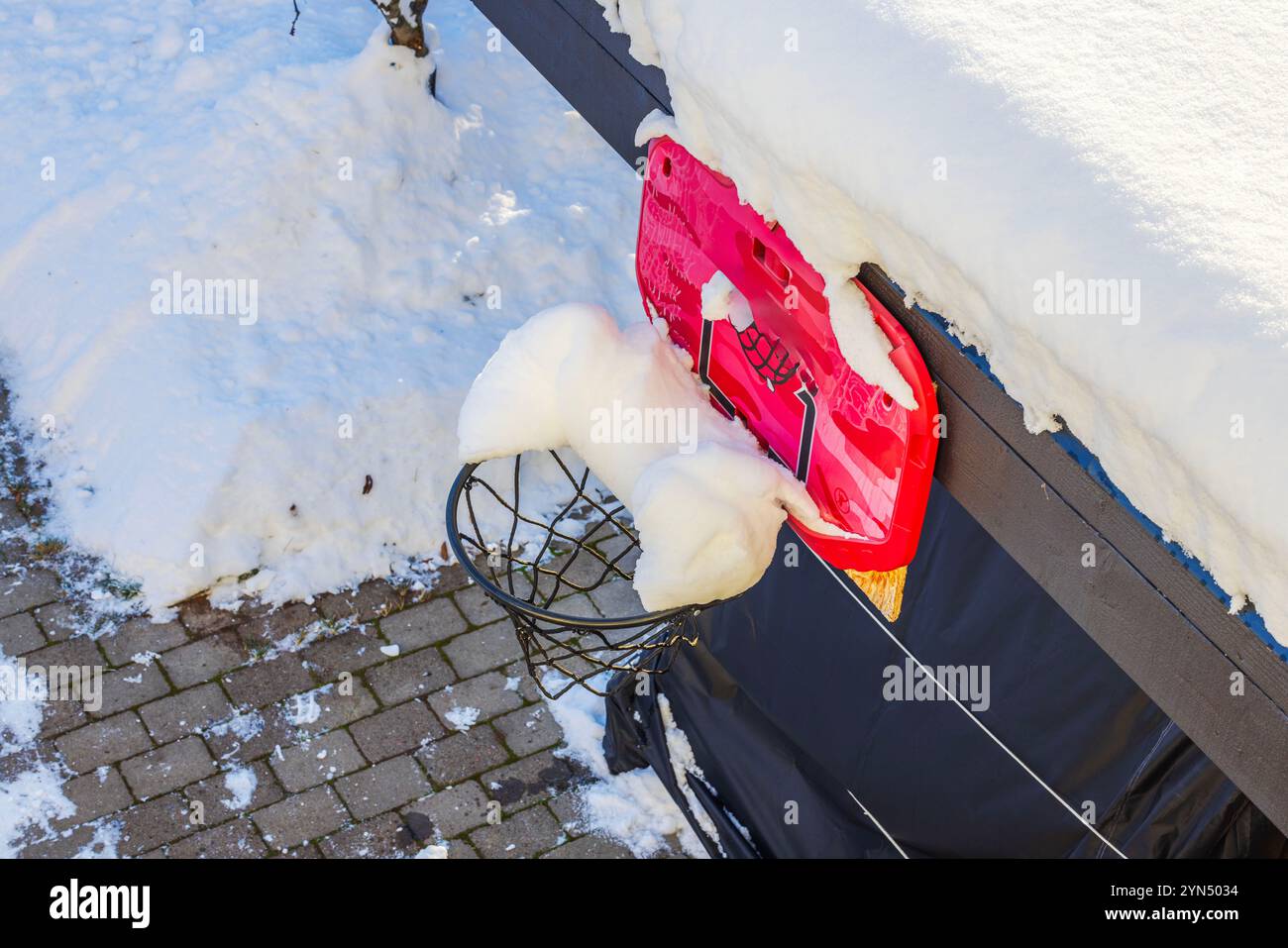 Snow-covered basketball hoop with red backboard attached to snowy roof ...