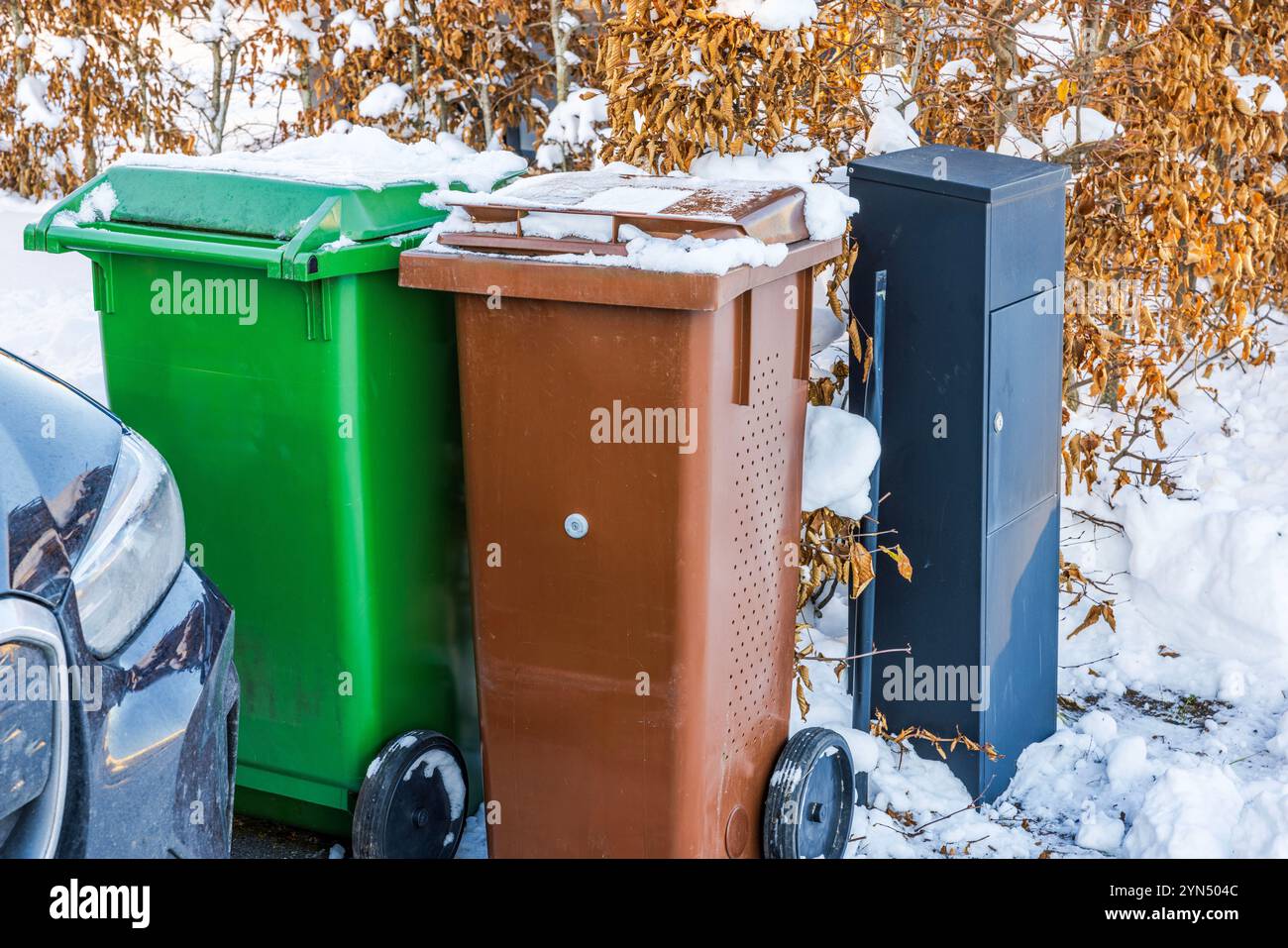Close-up of snow covered trash bins for sorting garbage next to black ...