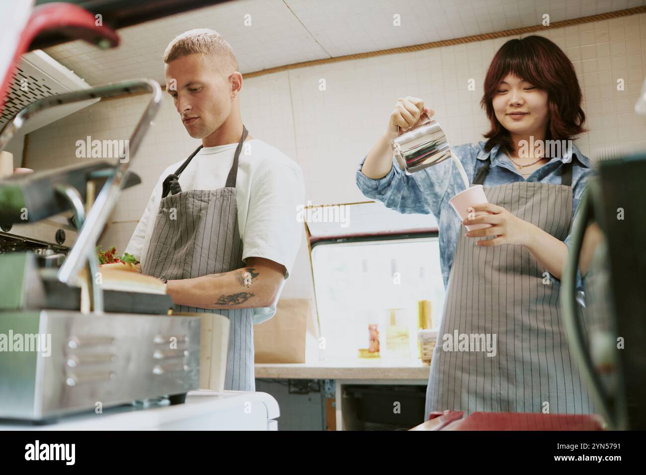 Low angle shot of smiling Asian female barista making cappuccino while ...