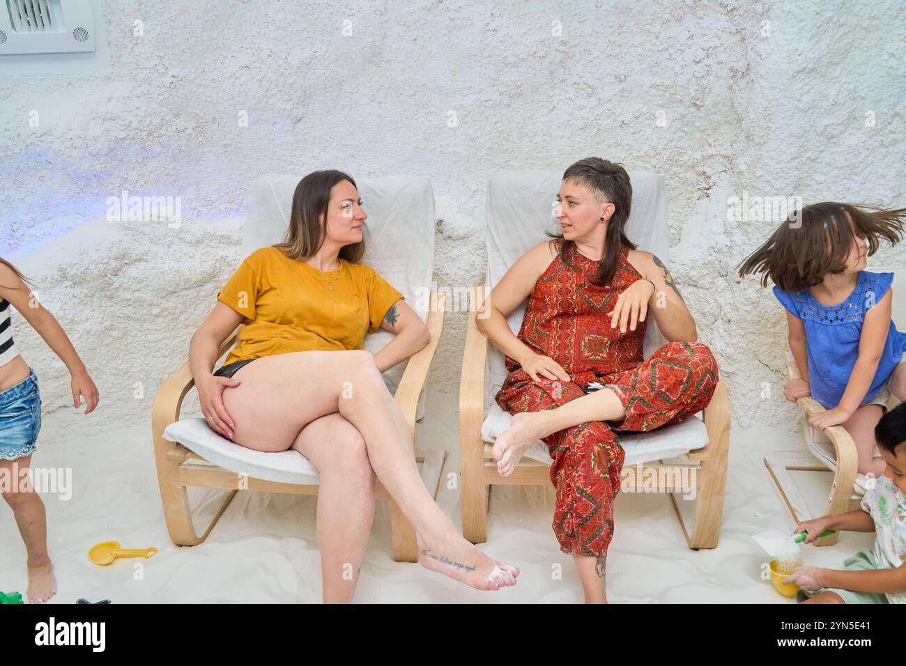 Two women relaxing and talking in a salt therapy room with children playing around Stock Photo ...