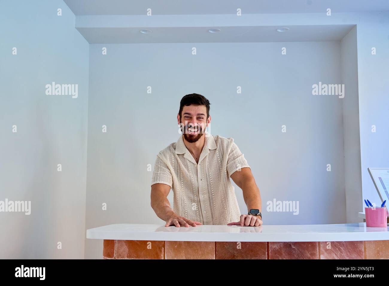 Man standing behind a reception desk, smiling warmly at the camera. The ...