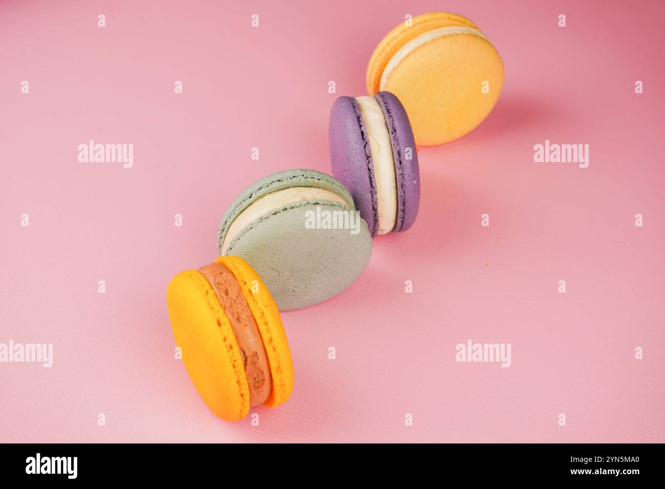 Bright and colorful macarons lined up on a surface with a pink ...