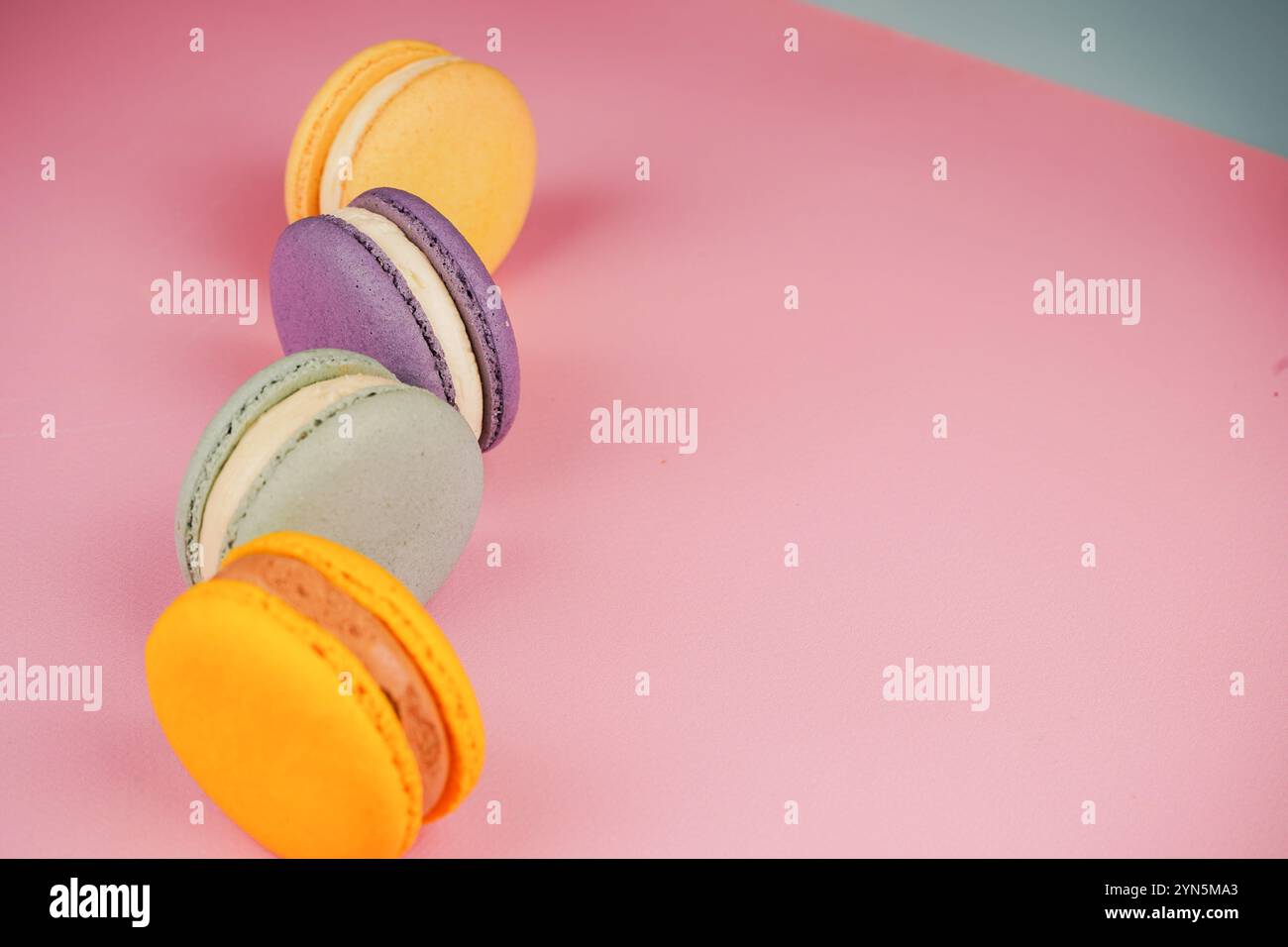 Bright and colorful macarons lined up on a surface with a pink ...