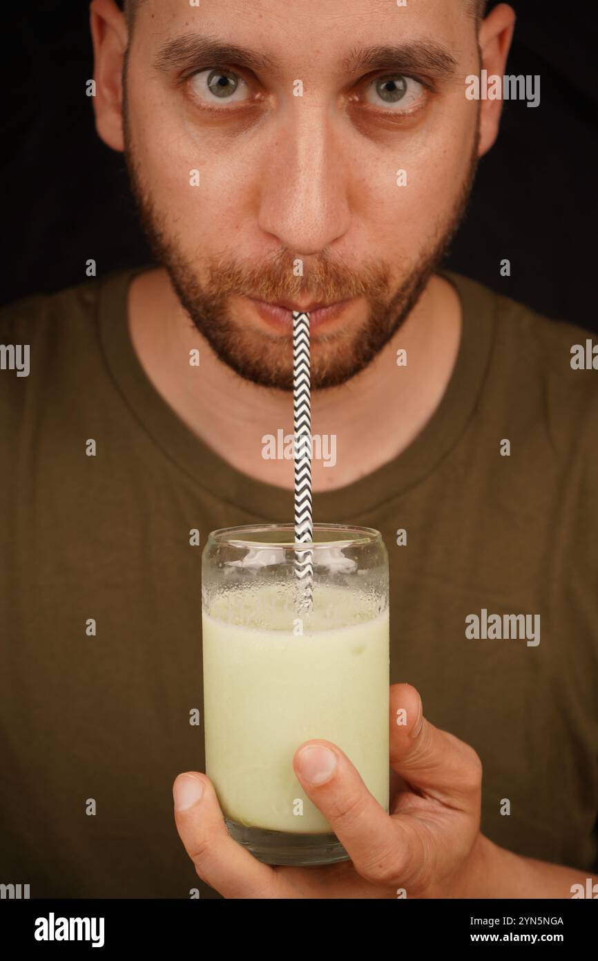 Close-up of a man drinking green matcha latte from a glass through a ...