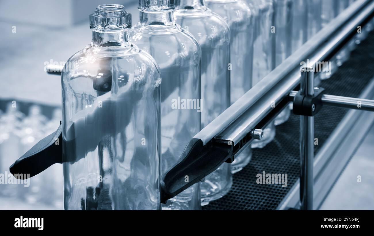 Glass bottles line on a conveyor belt. Bottles are transparent and ...