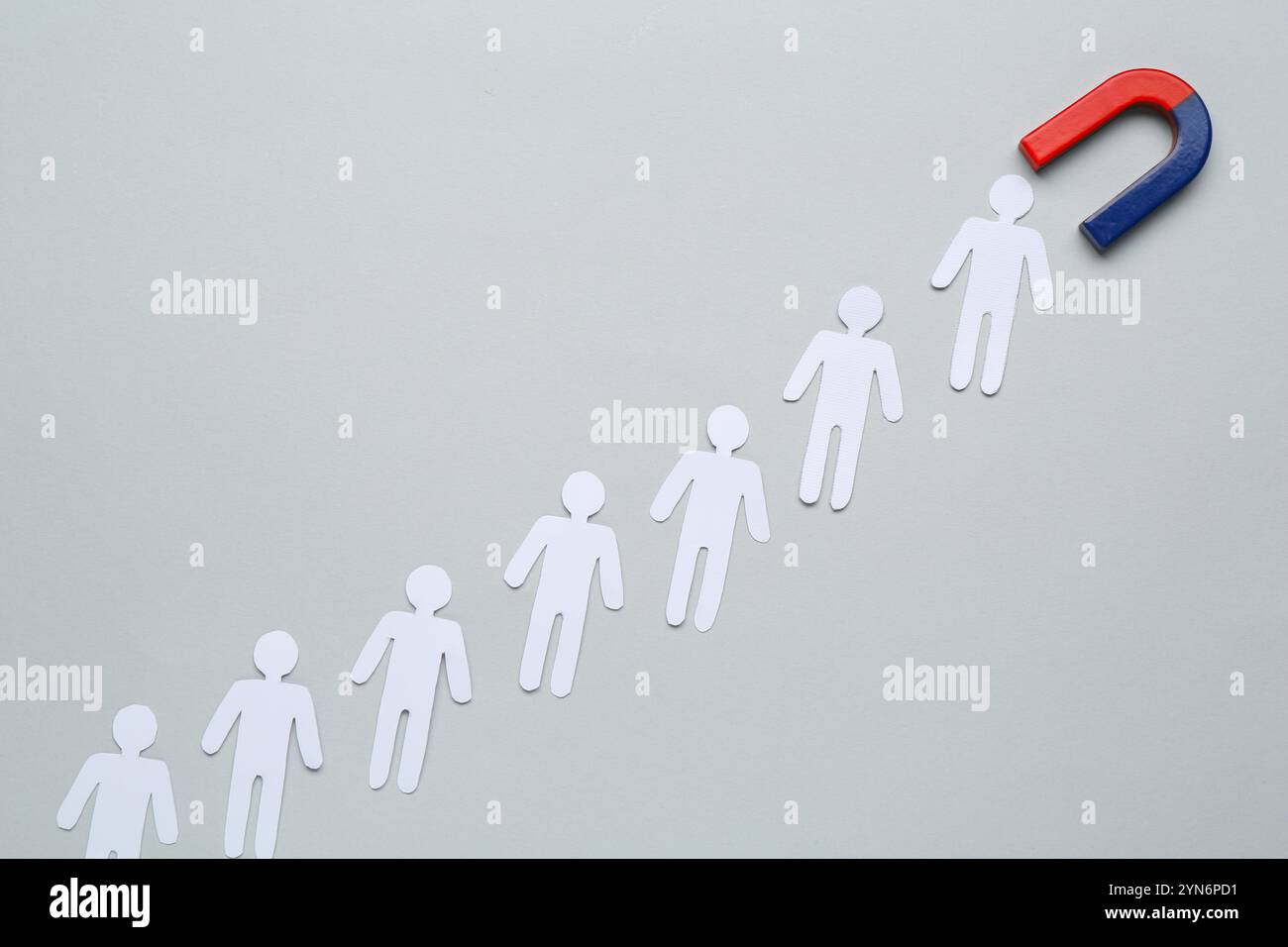 Magnet attracting paper cutouts of humans on light grey background ...