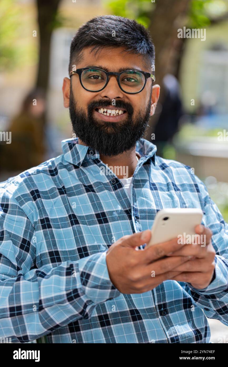 Indian bearded man using smartphone typing text messages in social media application online ...