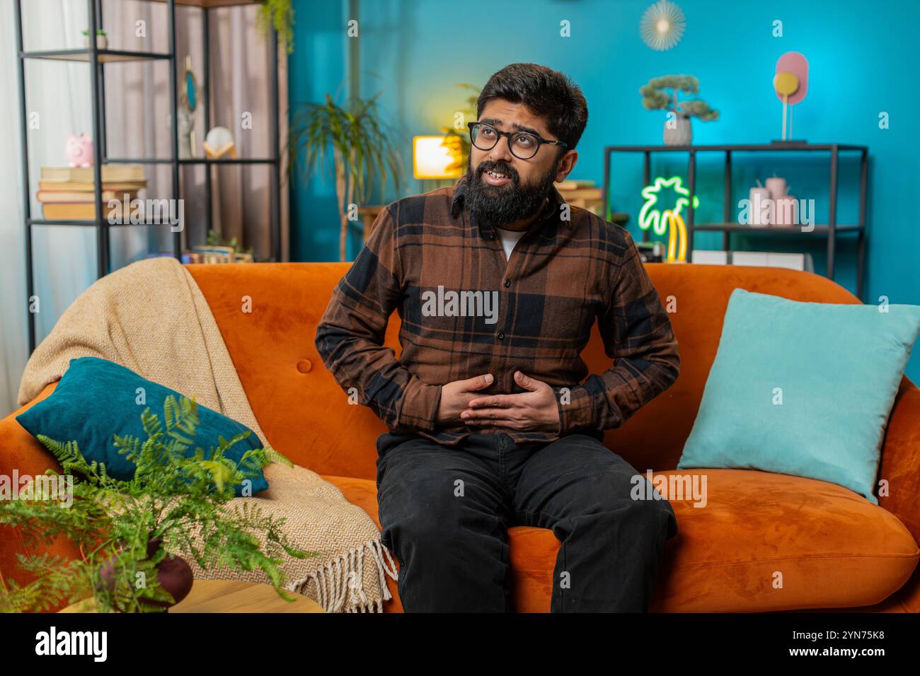 Indian young man sitting on sofa feeling sudden strong abdominal ...