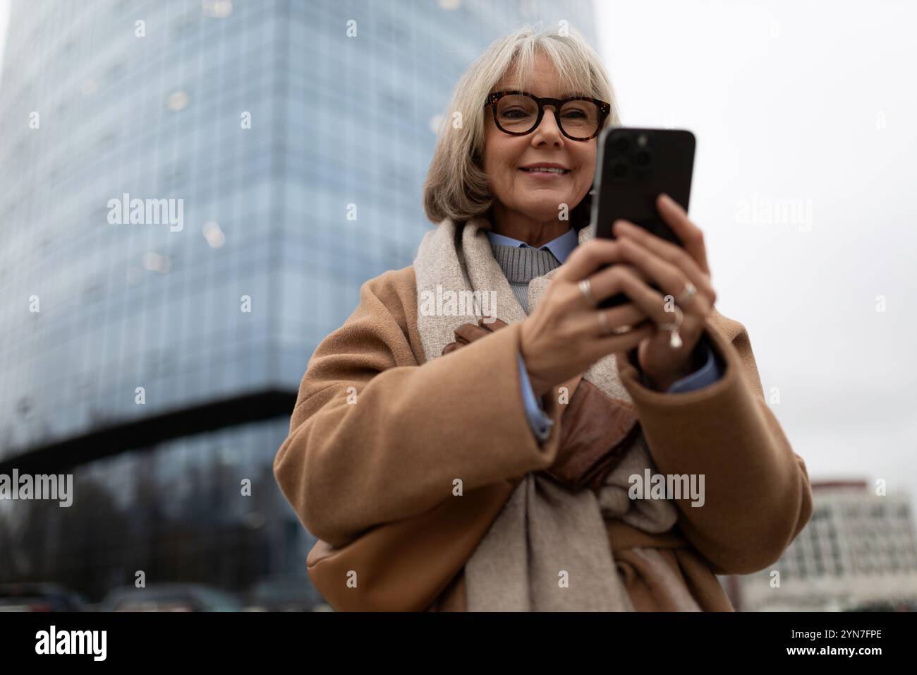 Older woman smiling while using smartphone in urban setting with modern ...