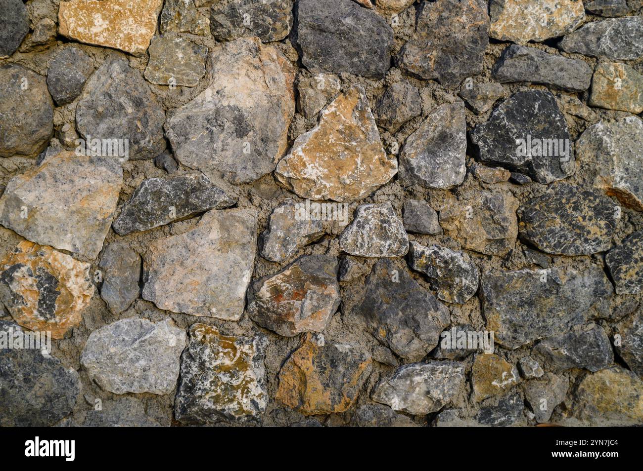 A wall made of various stones showcases a blend of colors and textures ...