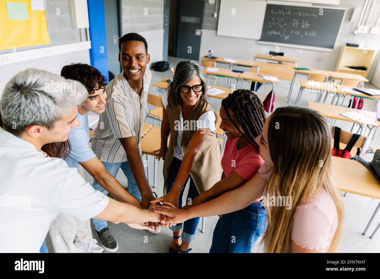 Diverse group of young students stacking hands with female teacher in ...