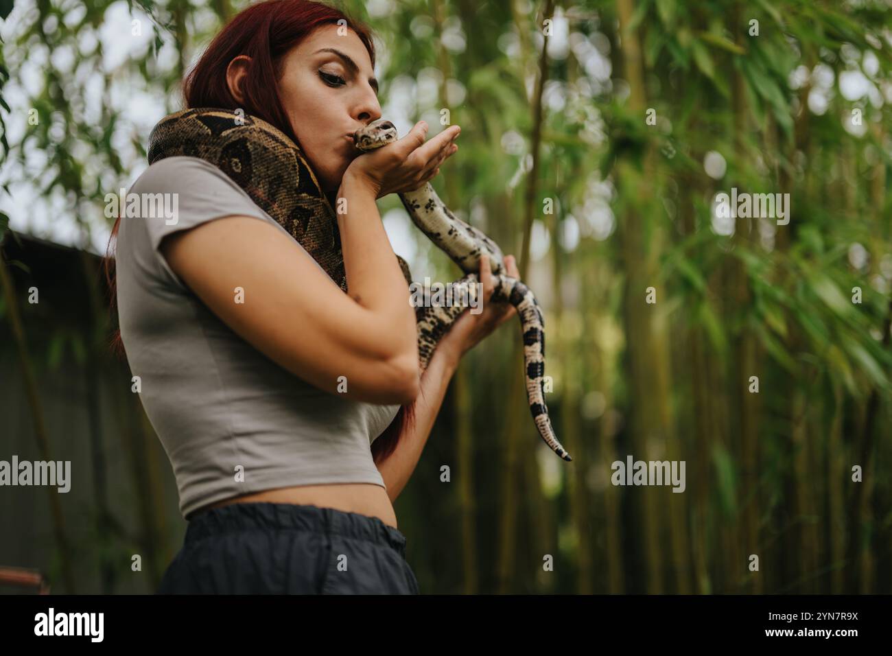 Girl with red hair gently holding a snake in lush garden Stock Photo ...