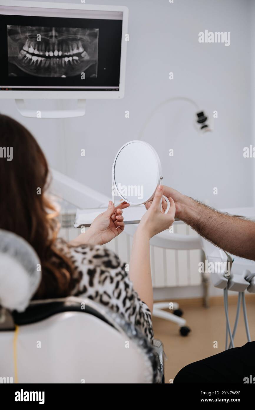 Dental patient with xray on screen, holding mirror during consultation ...