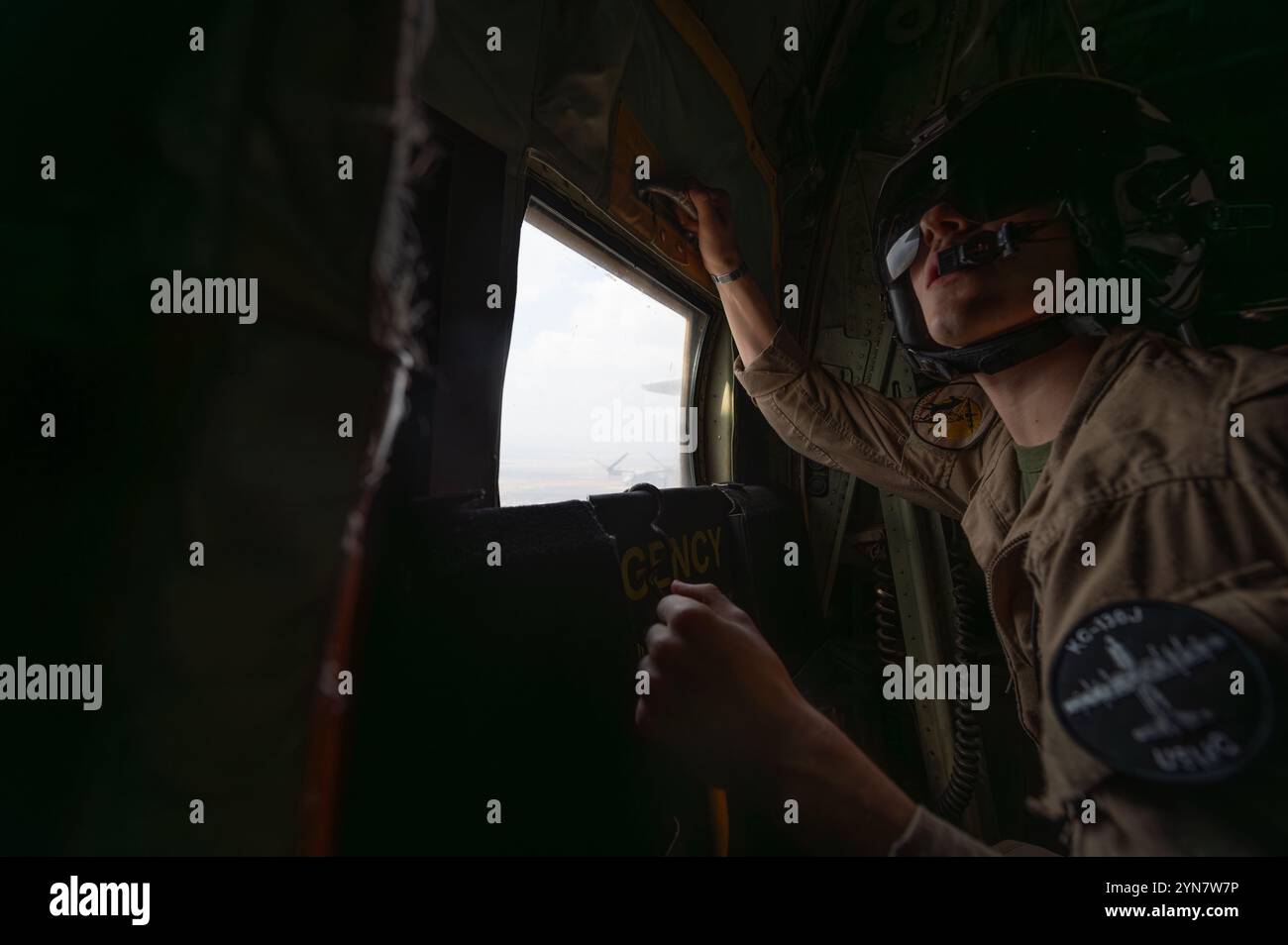 U.S. Marine Corps Loadmaster Corporal Casey Delapp peers out the window ...