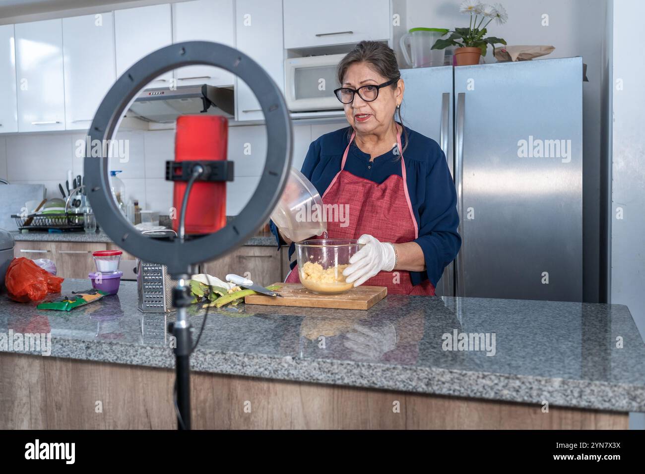 A woman is cooking in a kitchen with a red light on her phone. She is ...