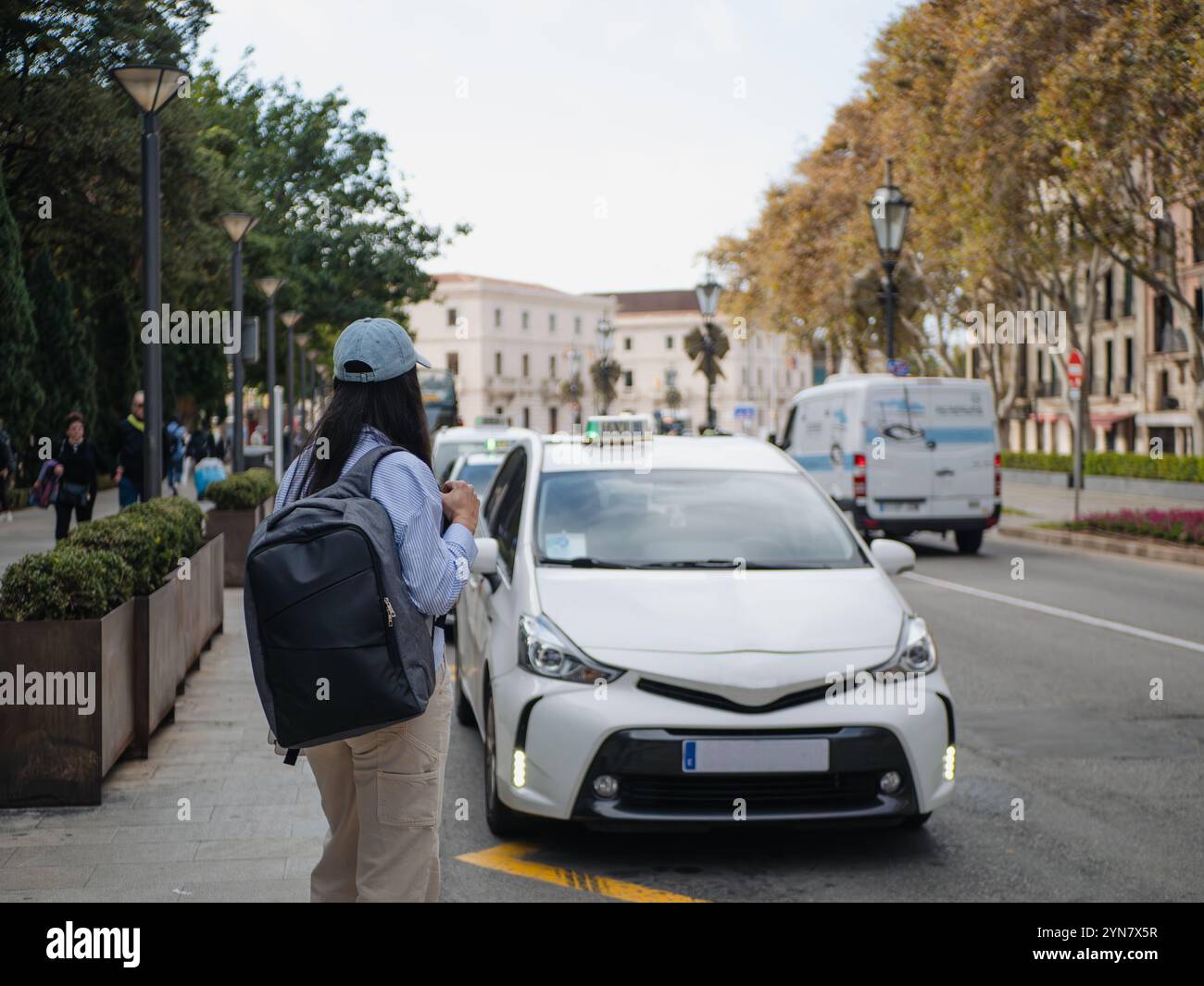 Back view of person with backpack hailing a taxi in busy city street ...